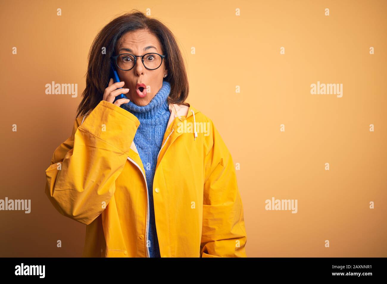 Middle age woman wearing yellow raincoat calling using smartphone ...