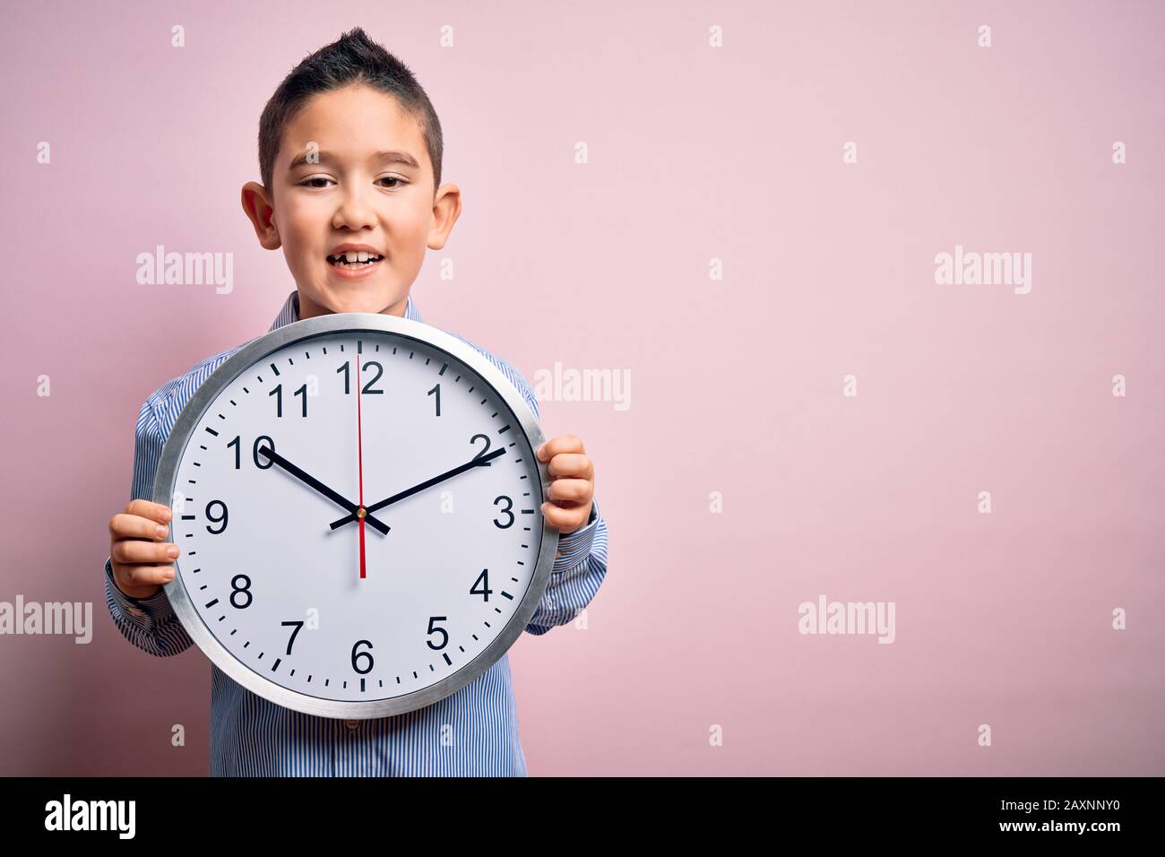Young little boy kid holding big minute clock over isolated pink ...