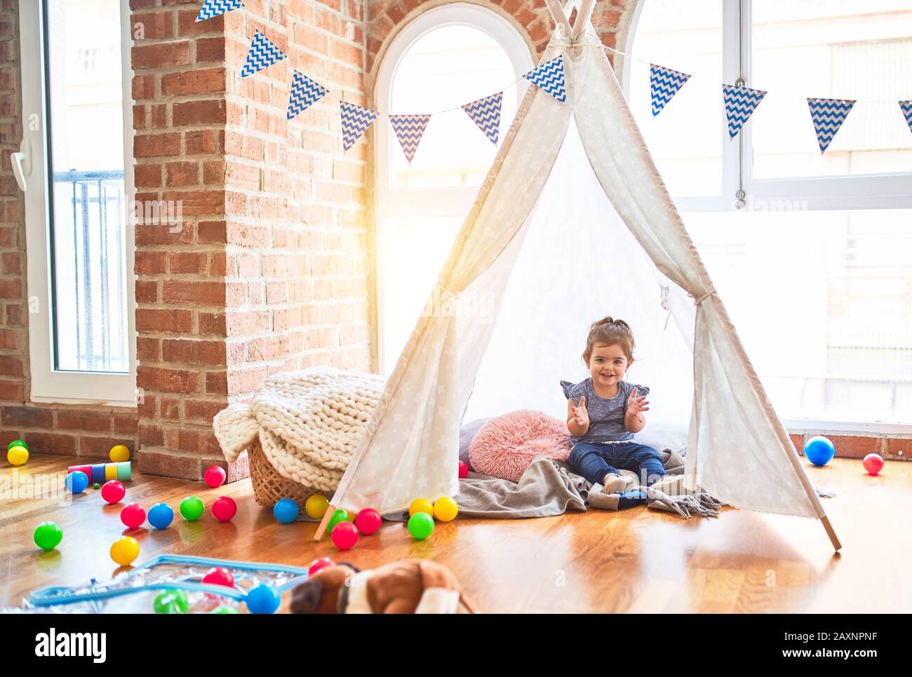 Beautiful toddler sitting on the floor inside tipi applauding and ...