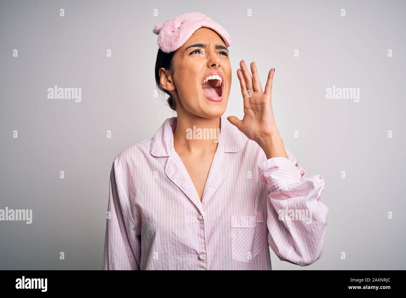 Young beautiful brunette woman wearing pajama and sleep mask over white ...