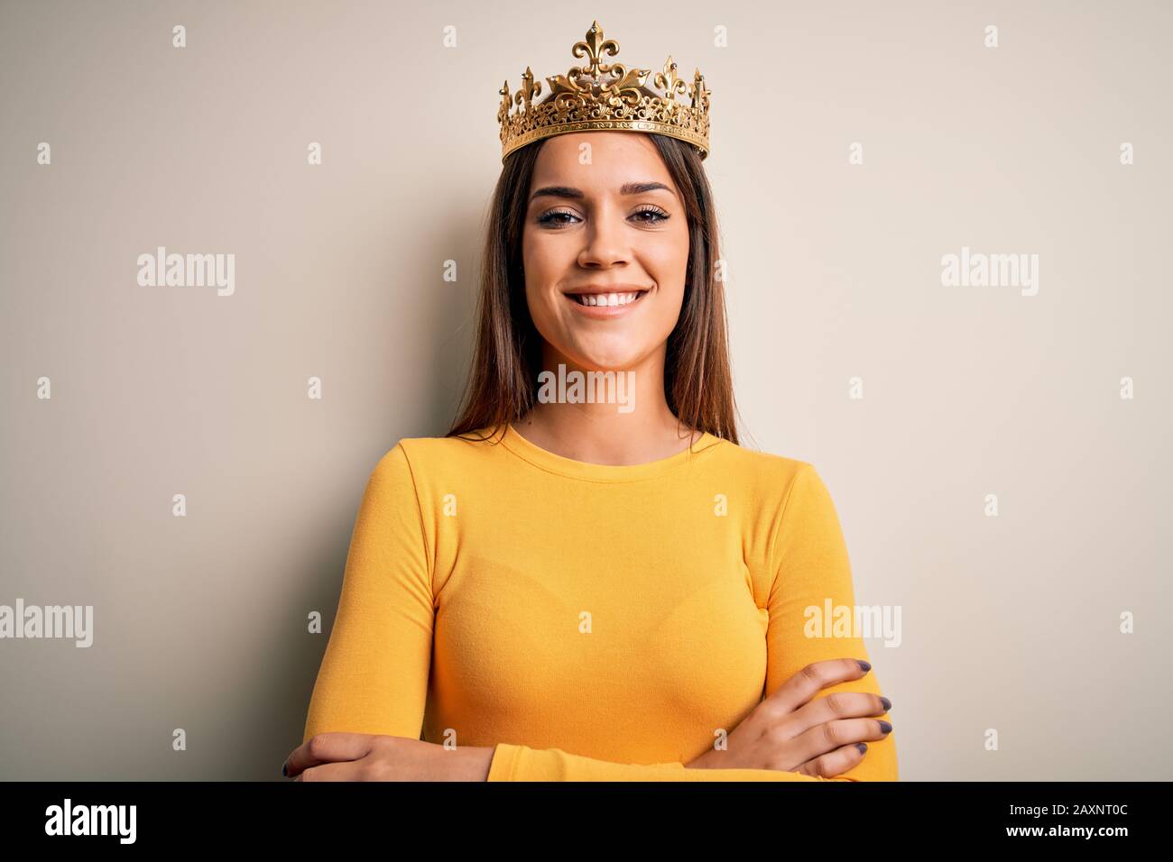 Young beautiful brunette woman wearing golden queen crown over white ...