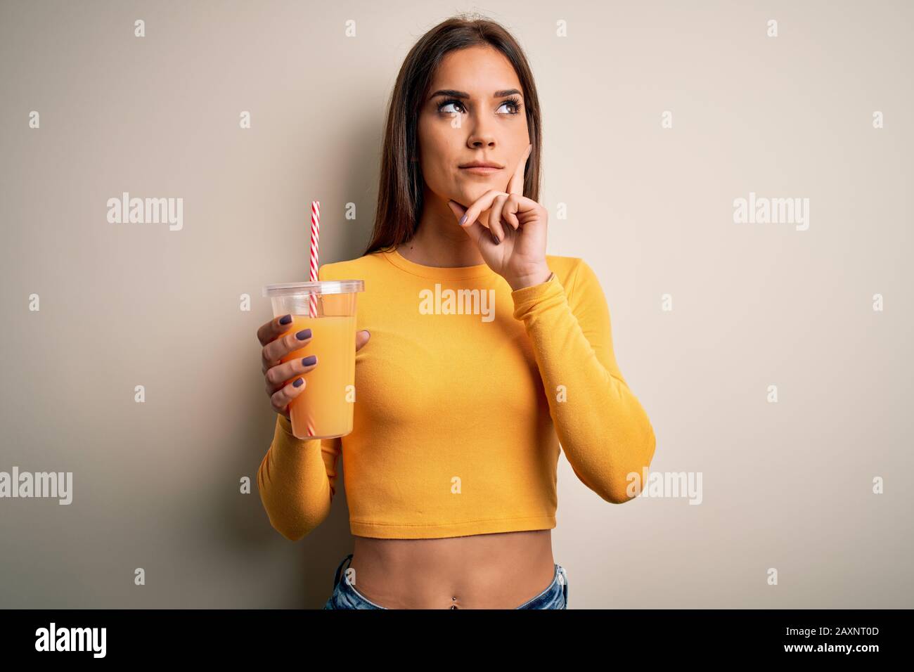 Young beautiful brunette woman drinking healthy orange juice over white ...