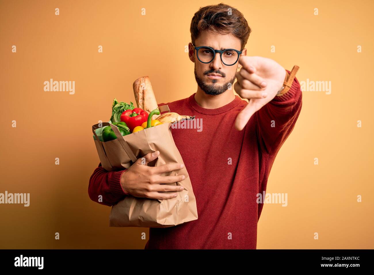 Young man wearing glasses holding paper bag with food over isolated ...