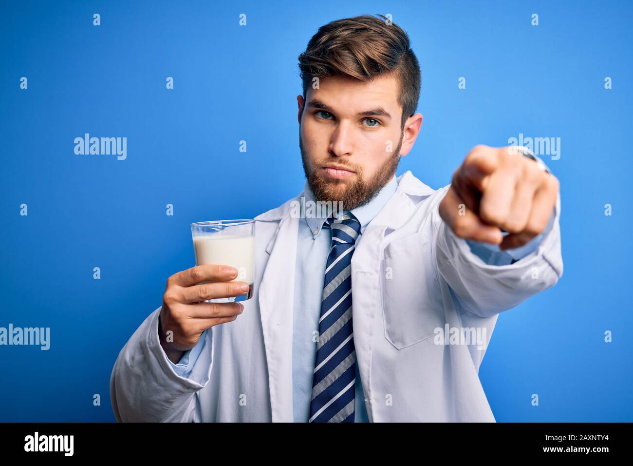 Young blond doctor man with beard and blue eyes wearing coat drinking ...