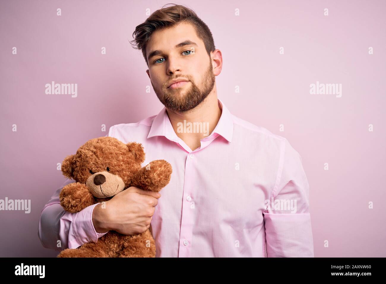 Young blond man with beard and blue eyes holding teddy bear toy over ...