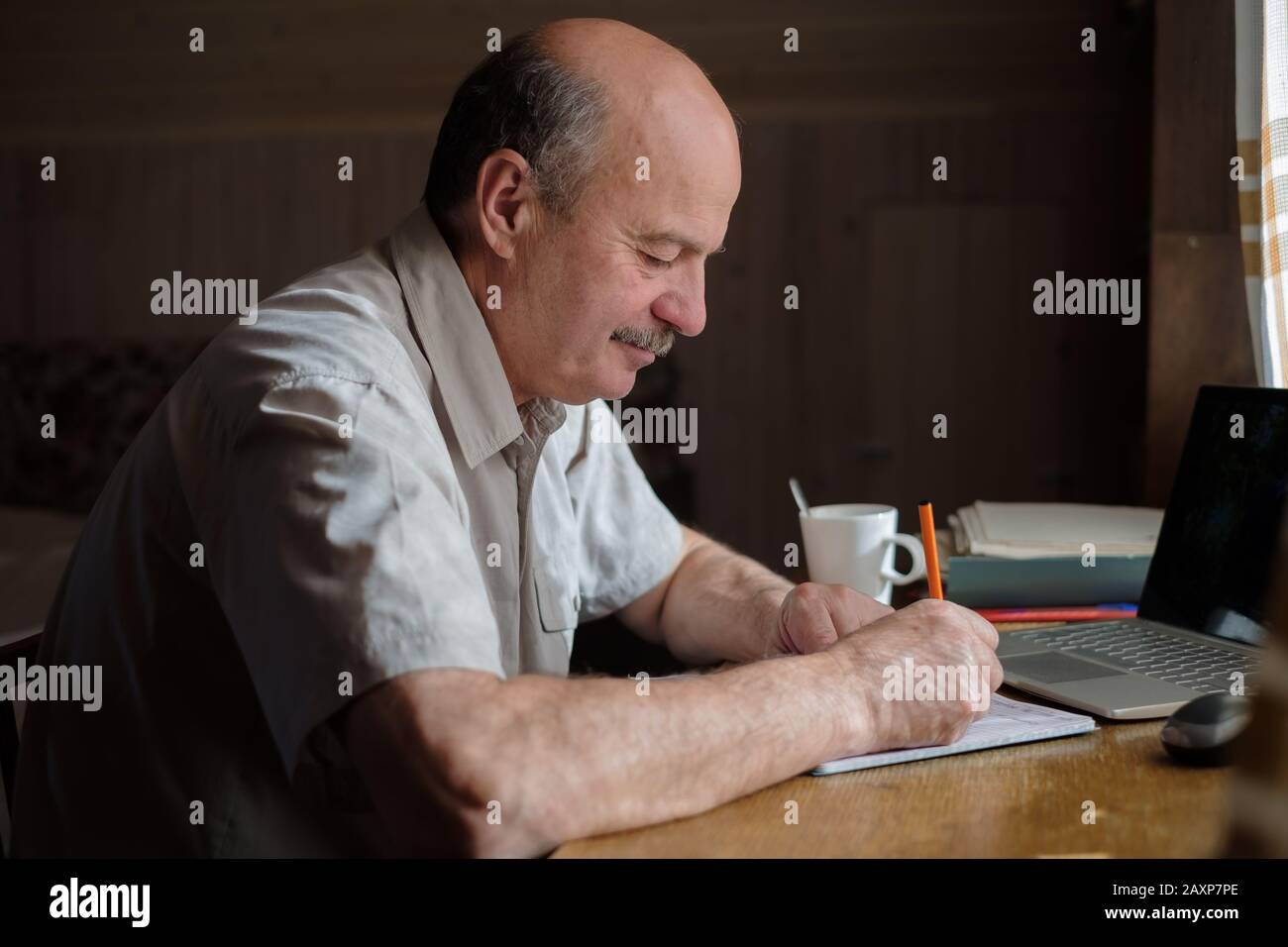 Senior man is writing in his room sitting near window. Diary concept ...