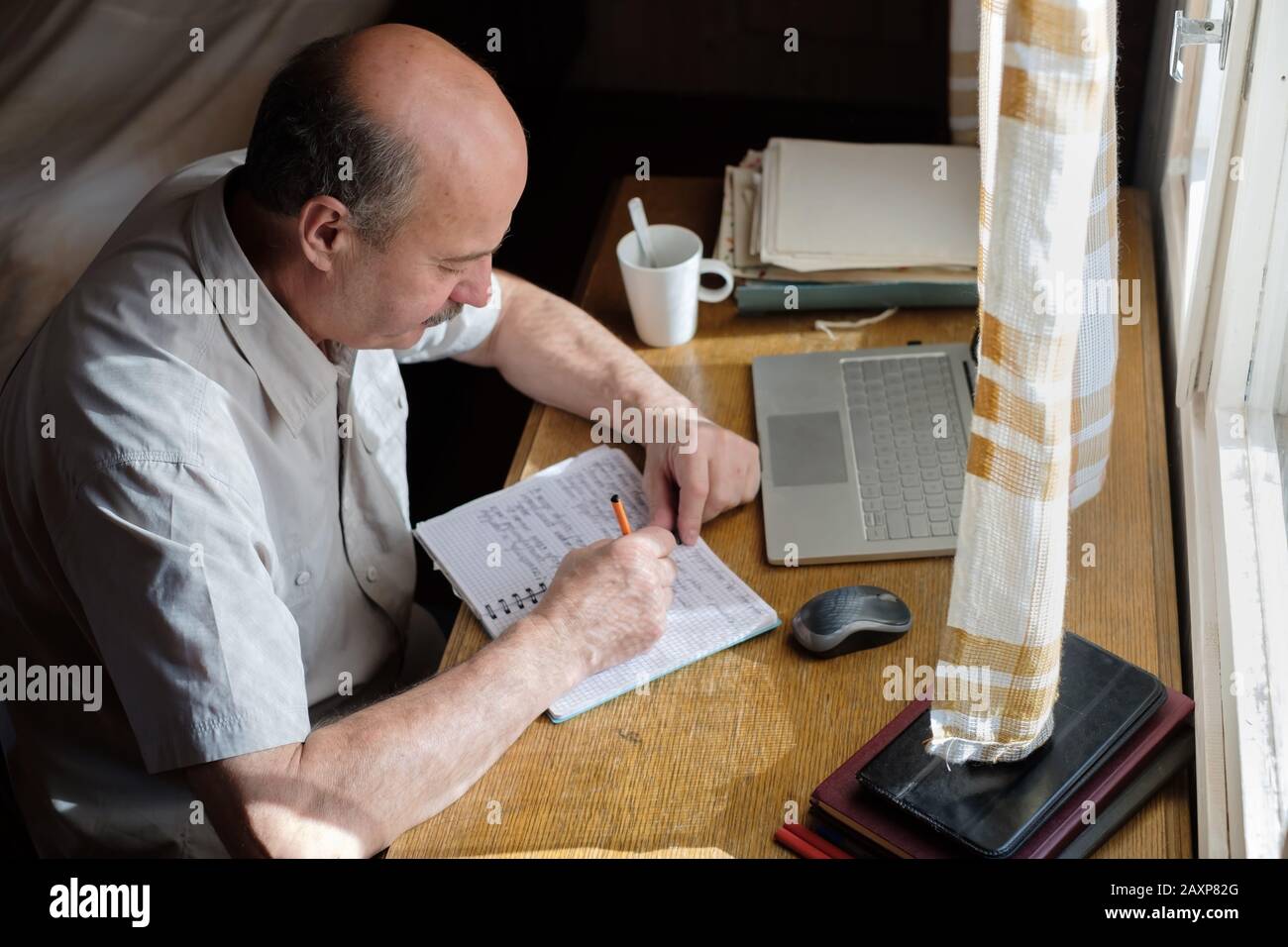 Senior man is writing in his room sitting near window. Diary concept ...
