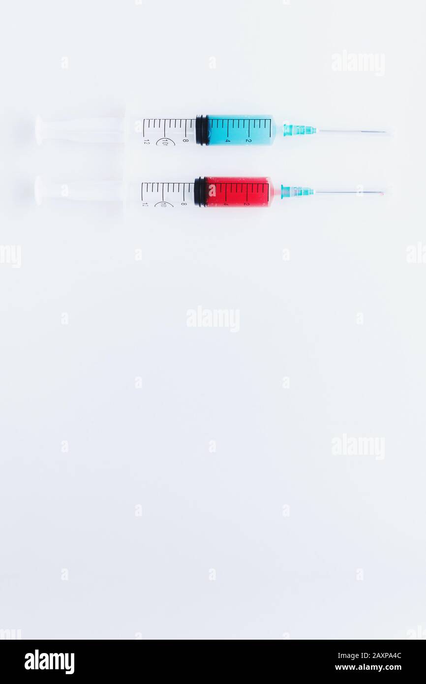 Two syringes filled with blue and red liquids on white background ...