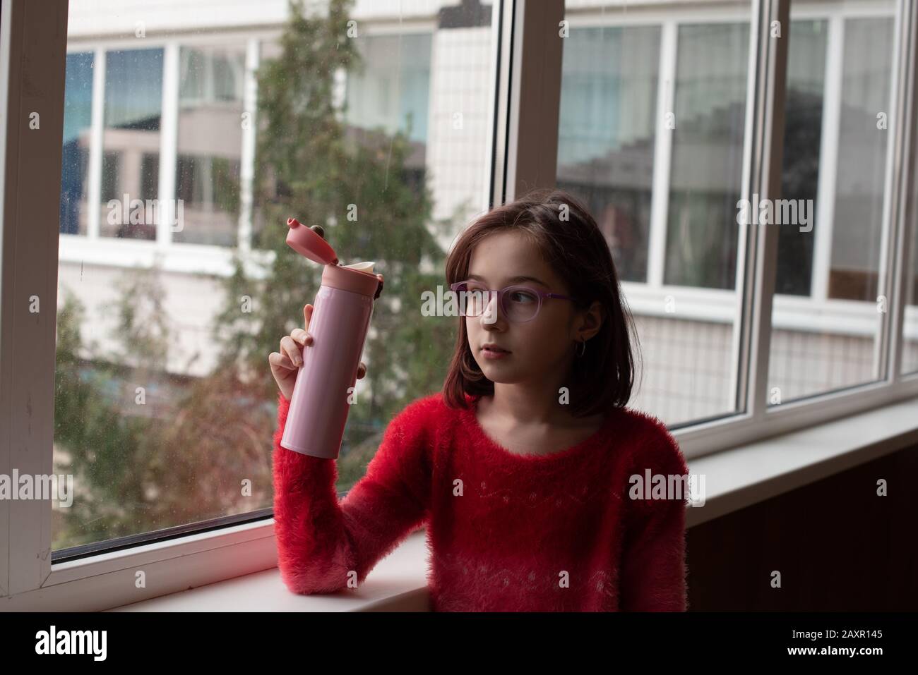 girl with cup. schoolgirl girl in glasses drinks water from a thermomug ...