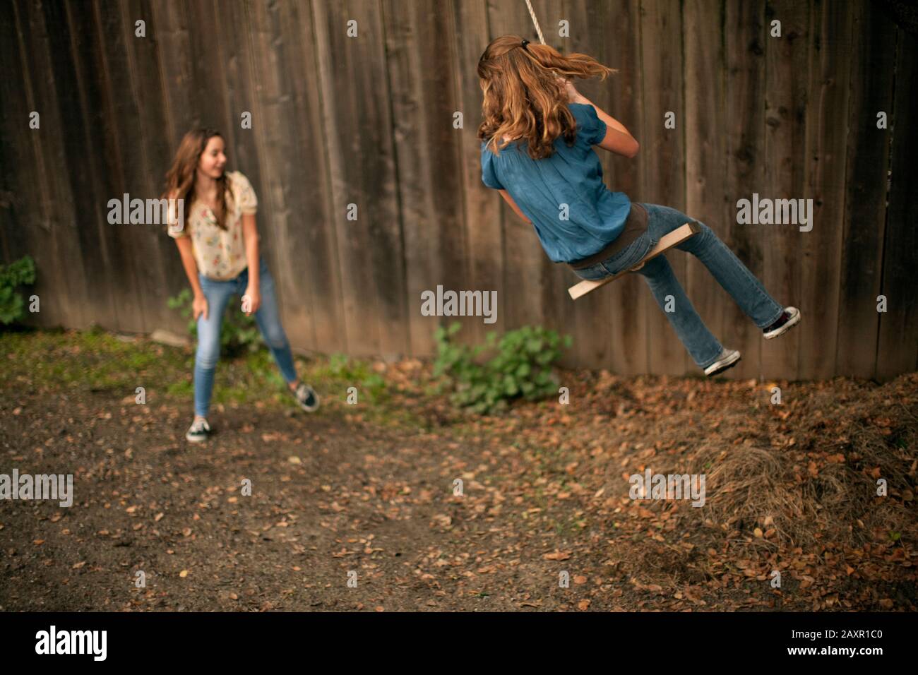 Two friends playing with rope swing in backyard Stock Photo - Alamy