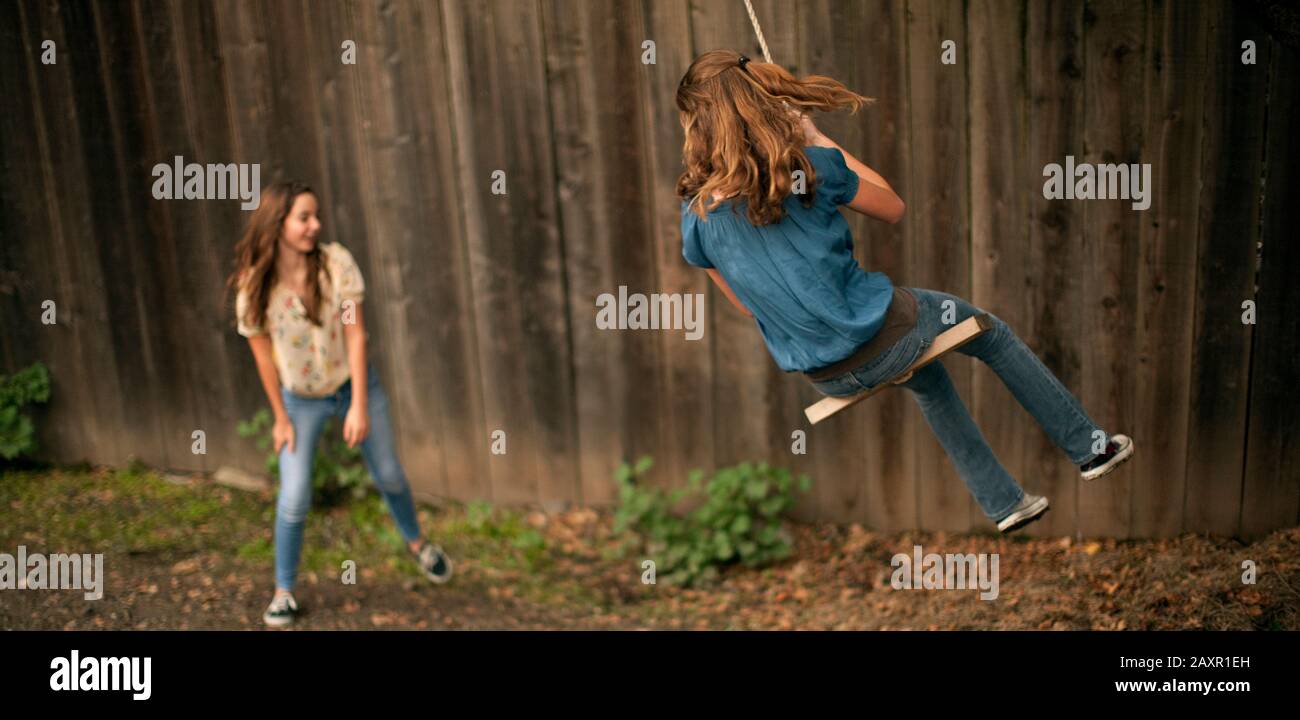 Two friends playing with rope swing in backyard Stock Photo - Alamy