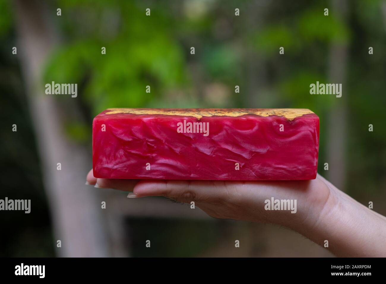 Casting red epoxy resin burl wood cube in hand at blurred background ...