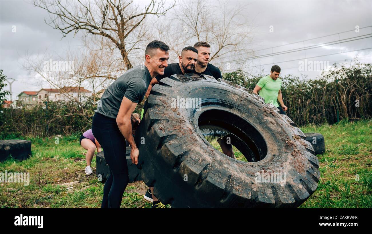 Participants in an obstacle course turning a wheel Stock Photo - Alamy