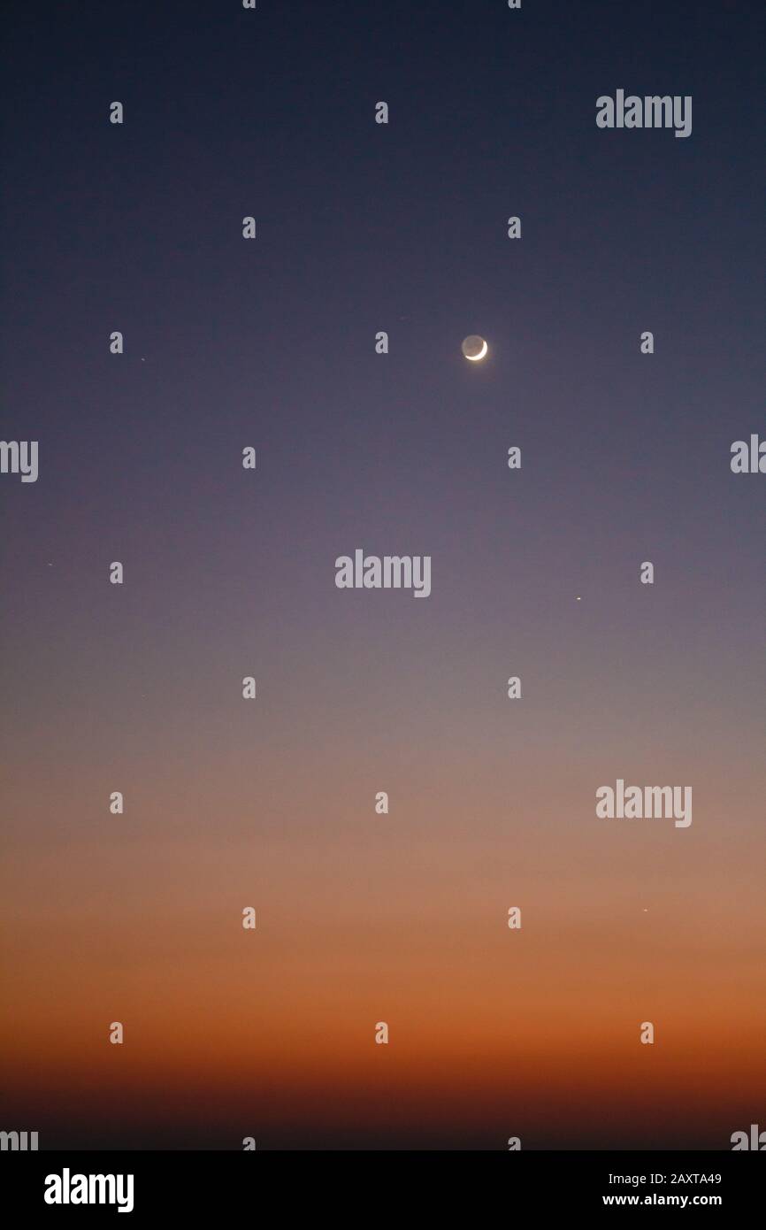 The crescent moon lit up by the sun as seen on a sunset sky with a ...