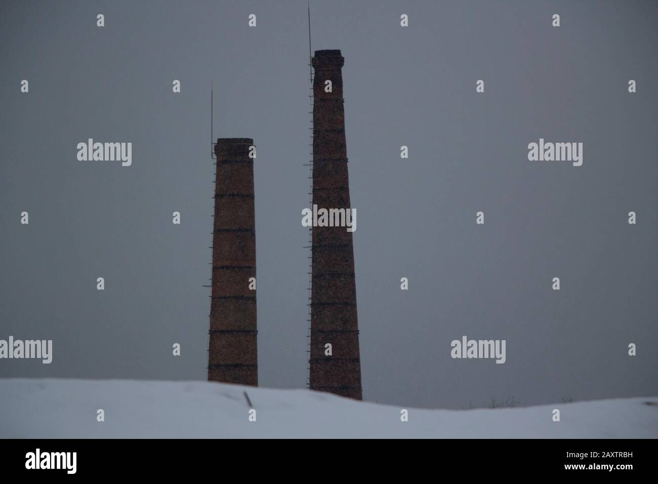 Pipes of a plant on a background of gray sky. Brick pipes peep out from ...