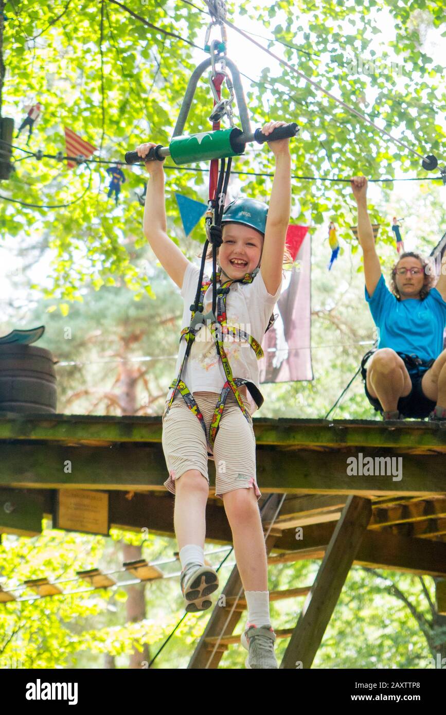 Young girl child kid on a zip wire zip lining in woodland forest tree ...