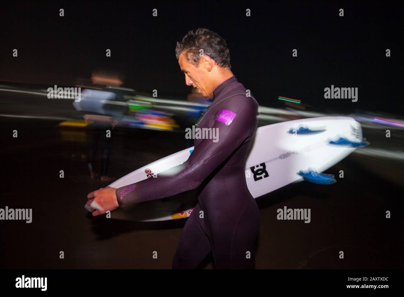 Surfers going surfing with neon surfboards at night Stock Photo - Alamy