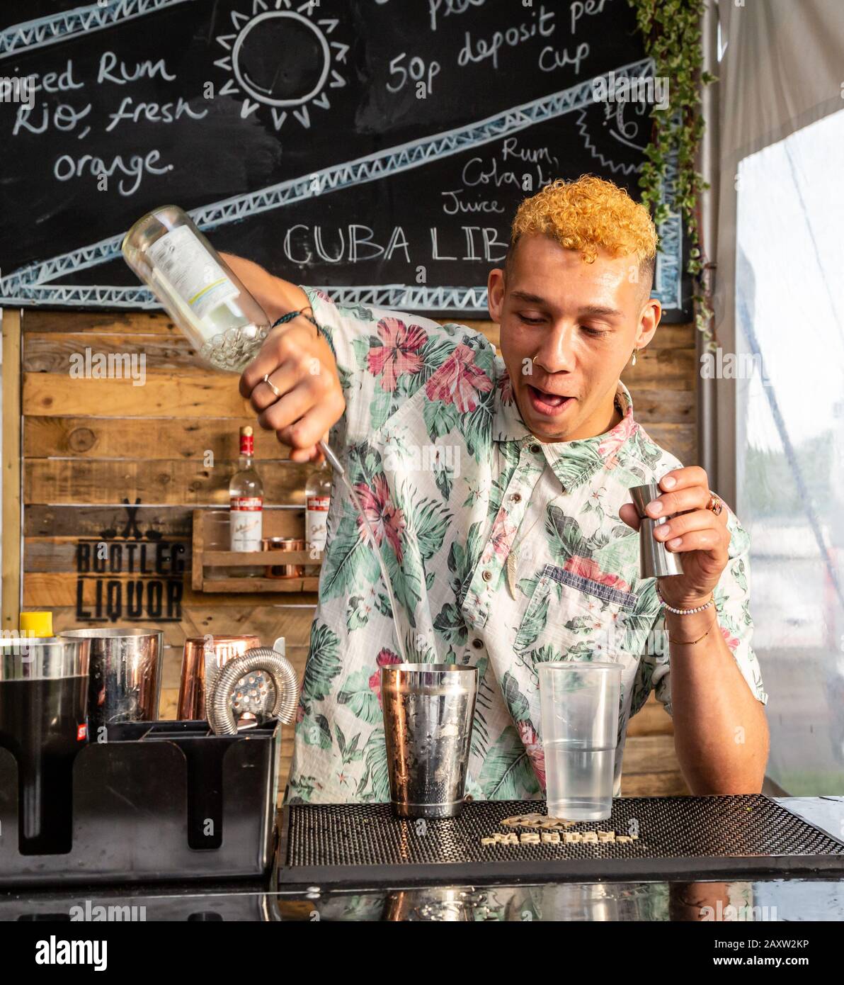 Young bartender in red & green floral shirt pouring liquor from height ...