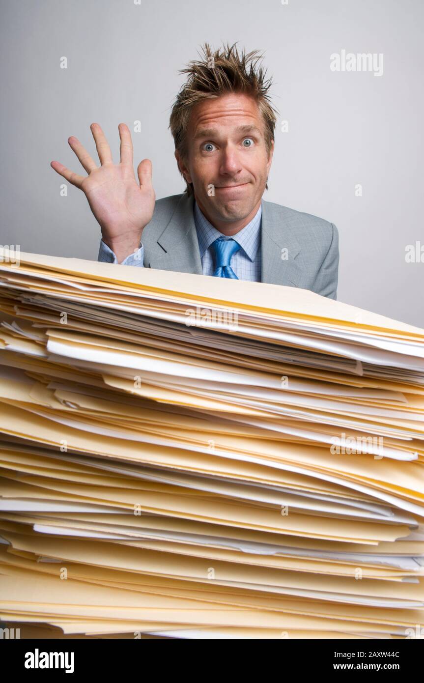 Cheerful businessman waving from behind a tall stack of paperwork on ...