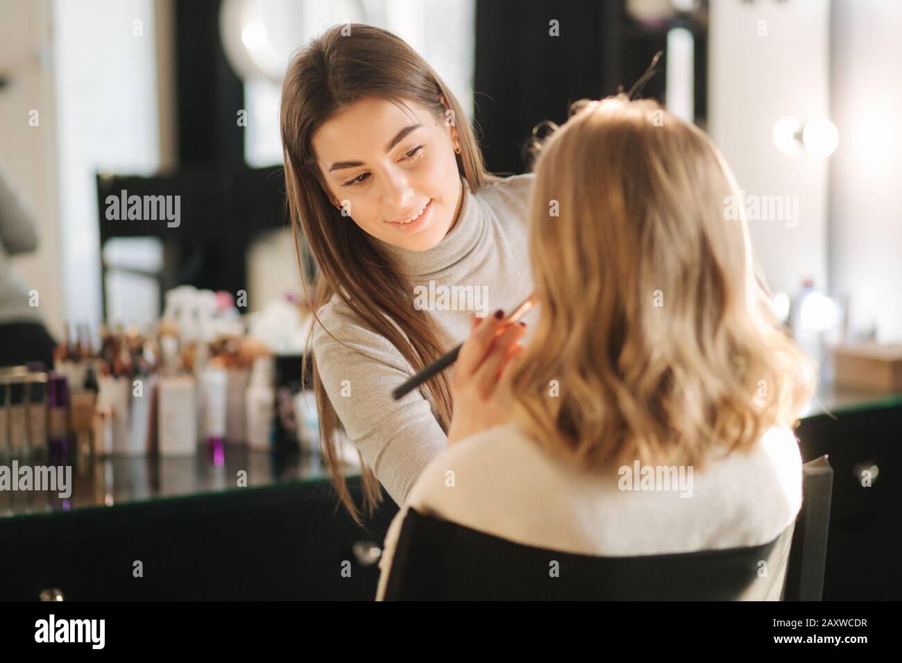 Beautiful female makeup artist doing makeup for a young blond hair girl ...