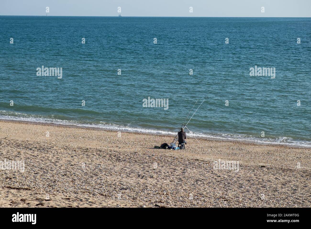 Man surf fishing, sitting on stool looking at the ocean and fishing ...