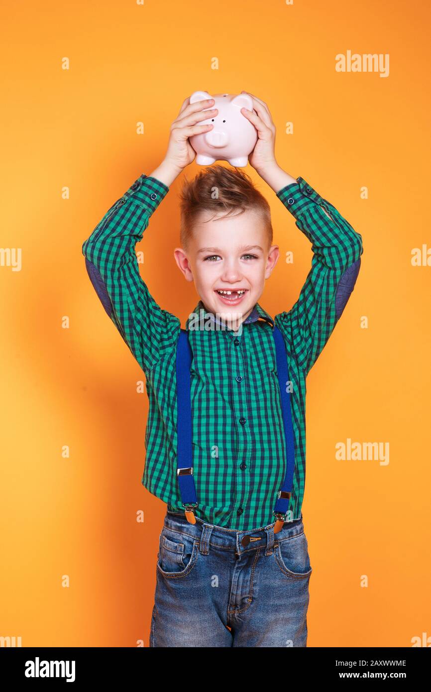Cute little boy shaking piggy box on orange background Stock Photo - Alamy