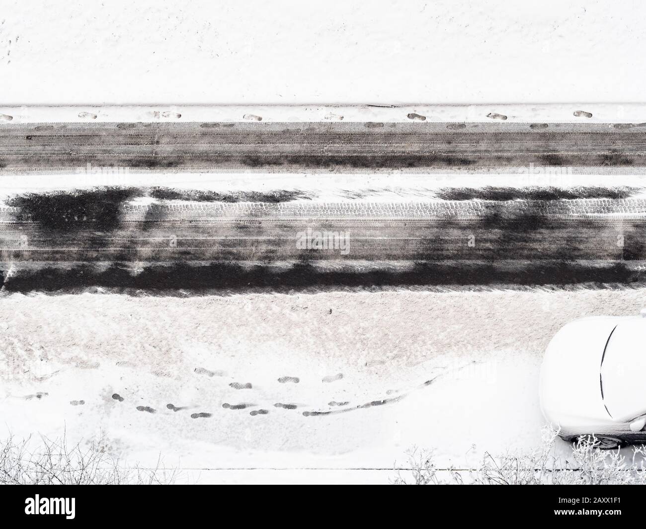 above view of footprints on snow-covered roadside of cleared urban road ...