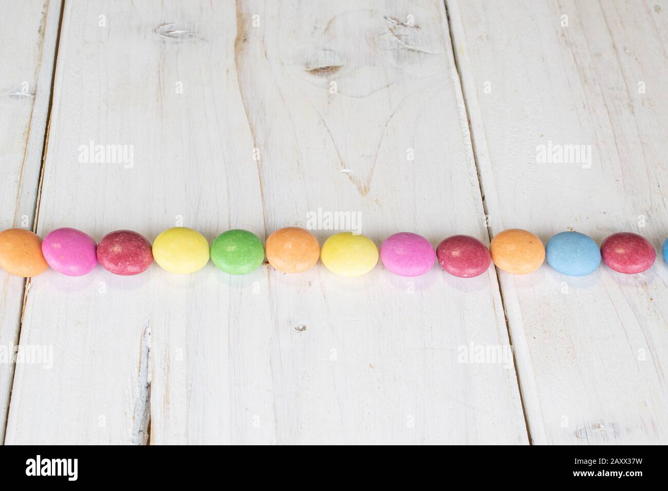 Lot of whole sweet colourful candy line on white wood Stock Photo - Alamy