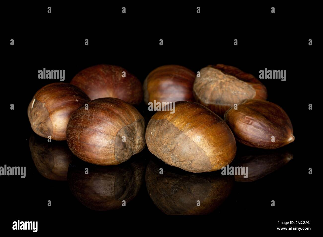 Group of seven whole edible brown chestnut ring isolated on black glass ...