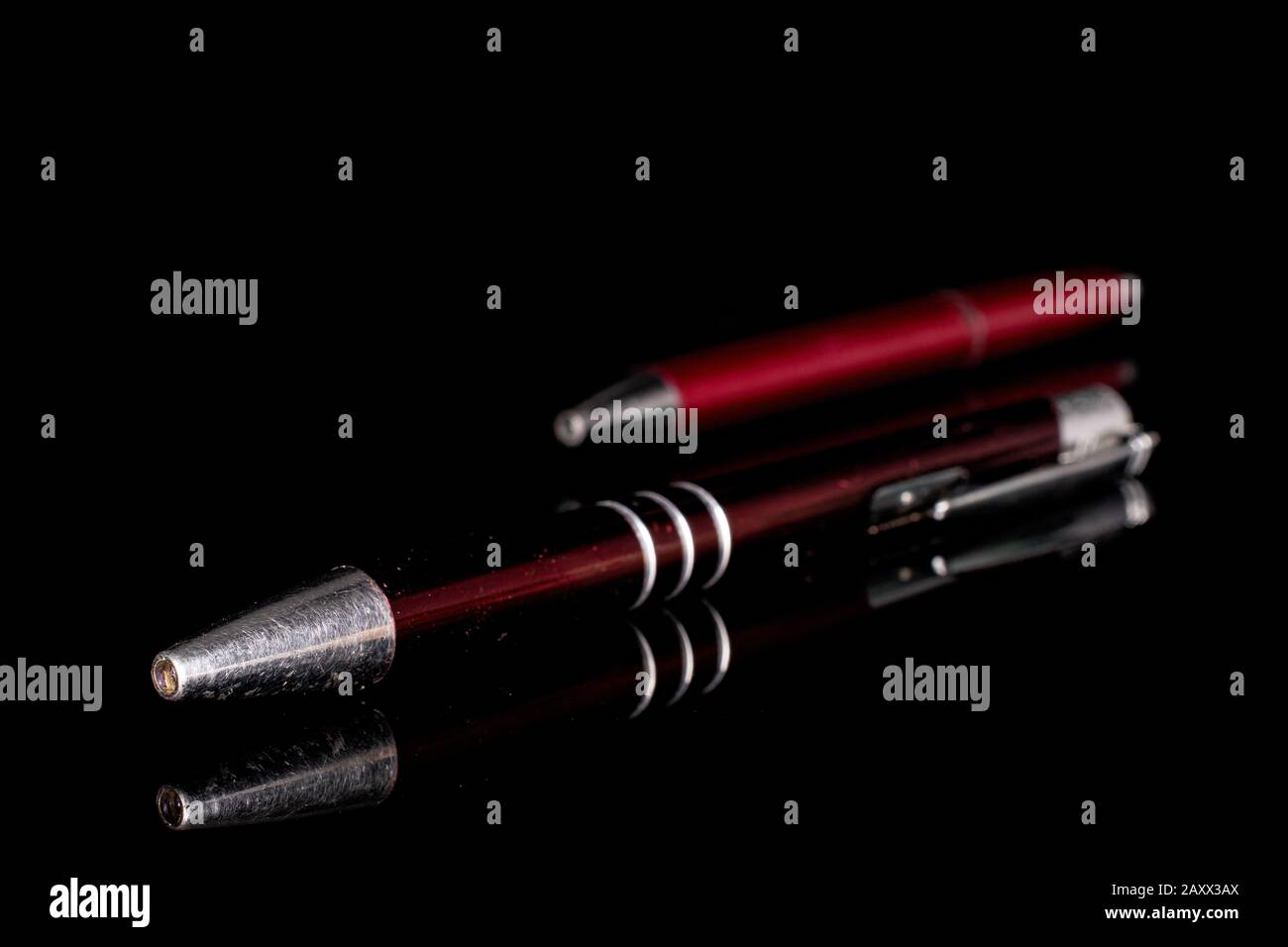 Group of two whole red writing ballpoint pen isolated on black glass ...