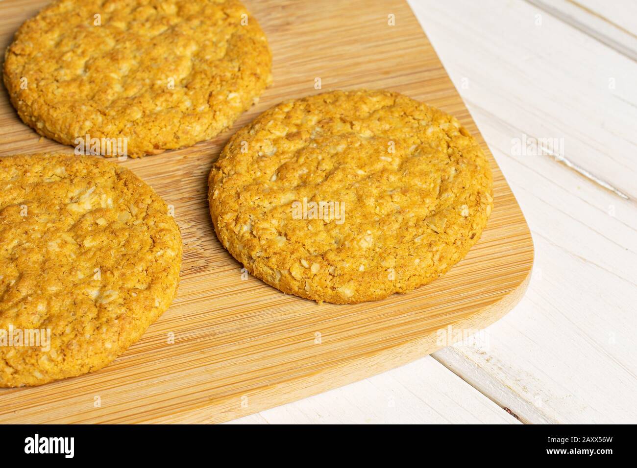 Group of three whole sweet golden oat cookie on bamboo cutting board on ...