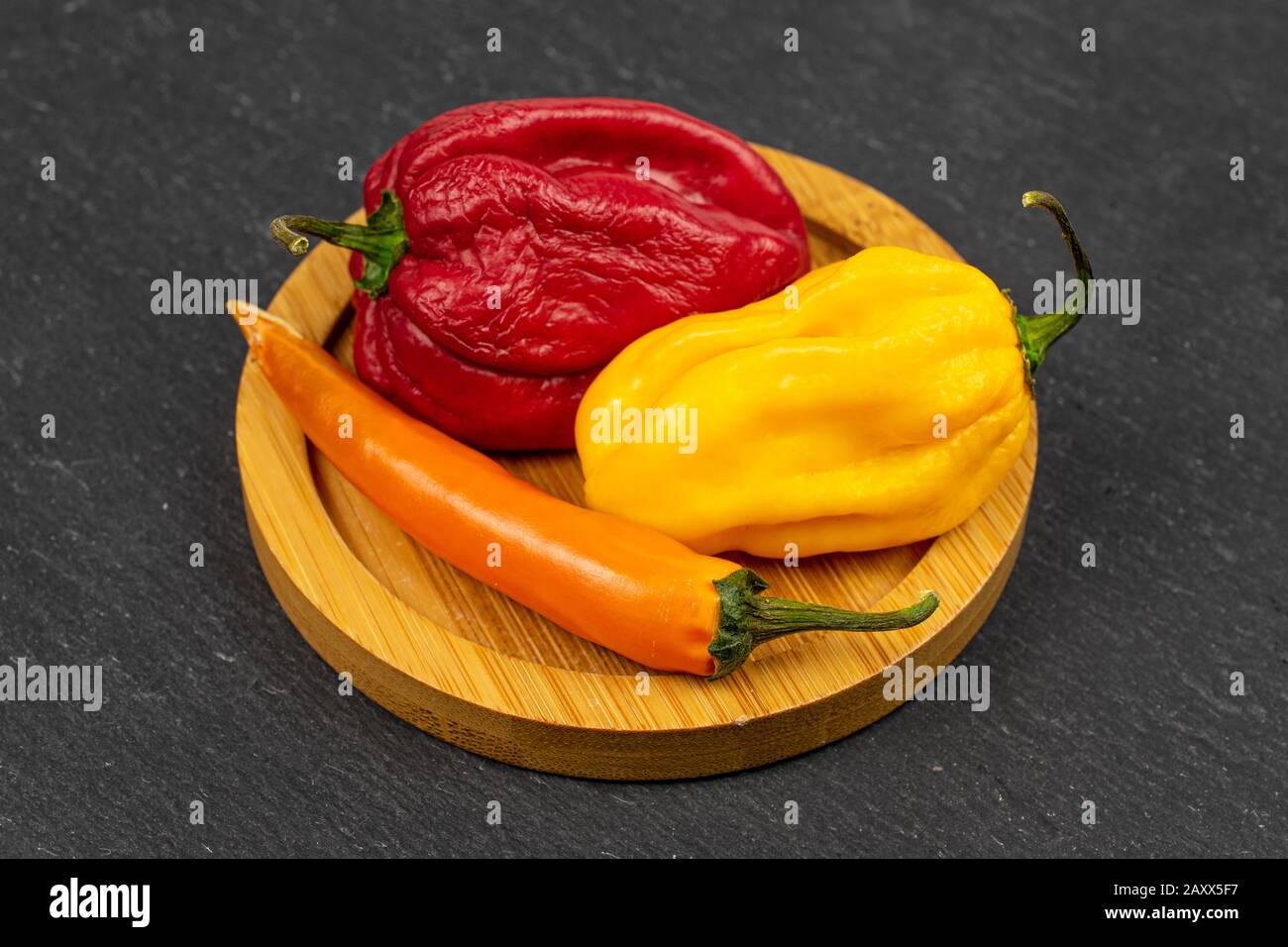Group of three whole hot chili pepper on bamboo coaster on grey stone ...