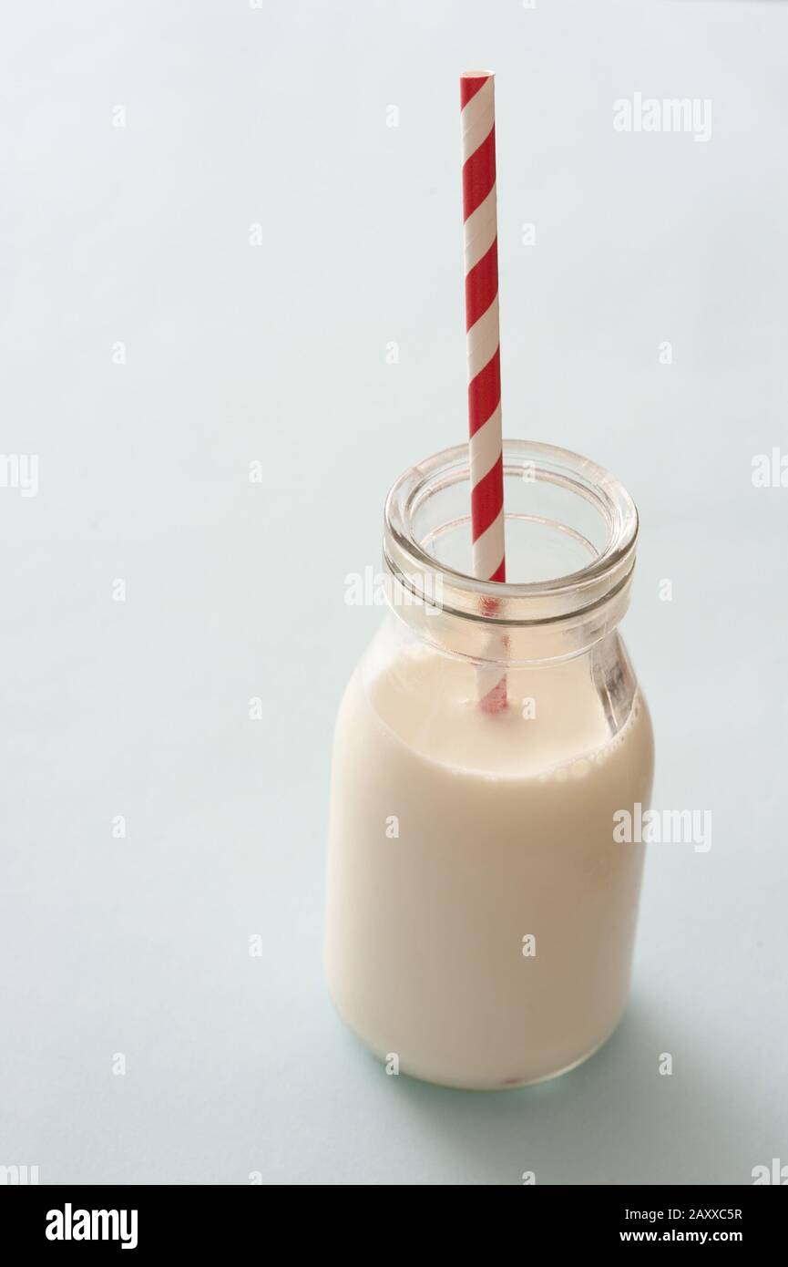 Little jar of milk with red and white straw stuck on top over neutral ...