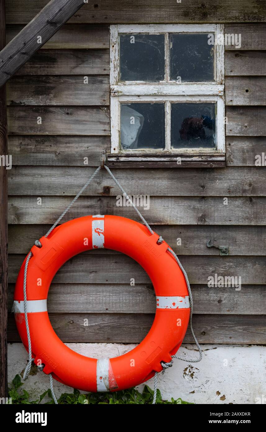 an orange coloured plastic lifebuoy on the side of an old wooden beach ...