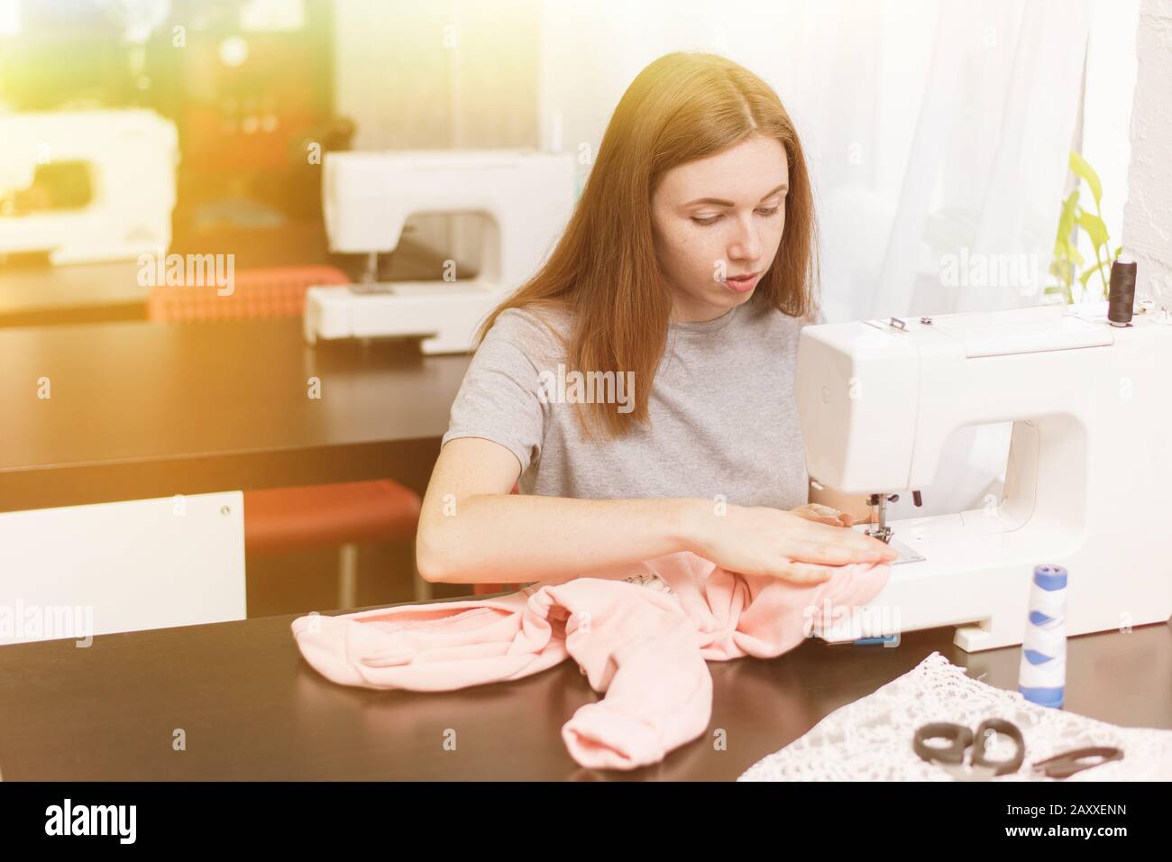 A beautiful seamstress works at a sewing machine. Cute girl sews a ...