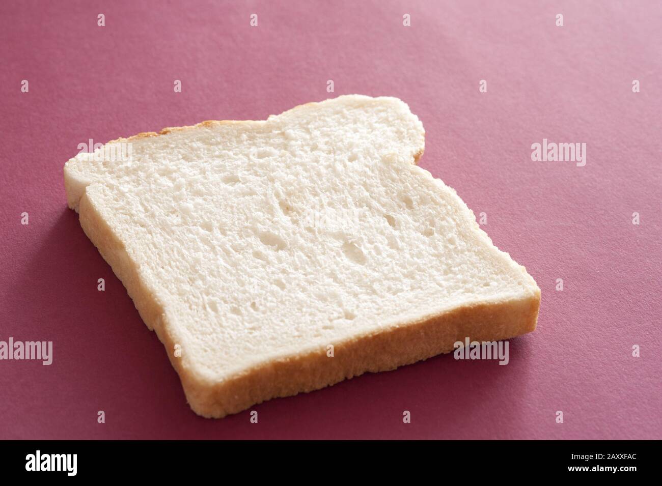Slice of plain fresh white bread on a maroon background viewed low ...