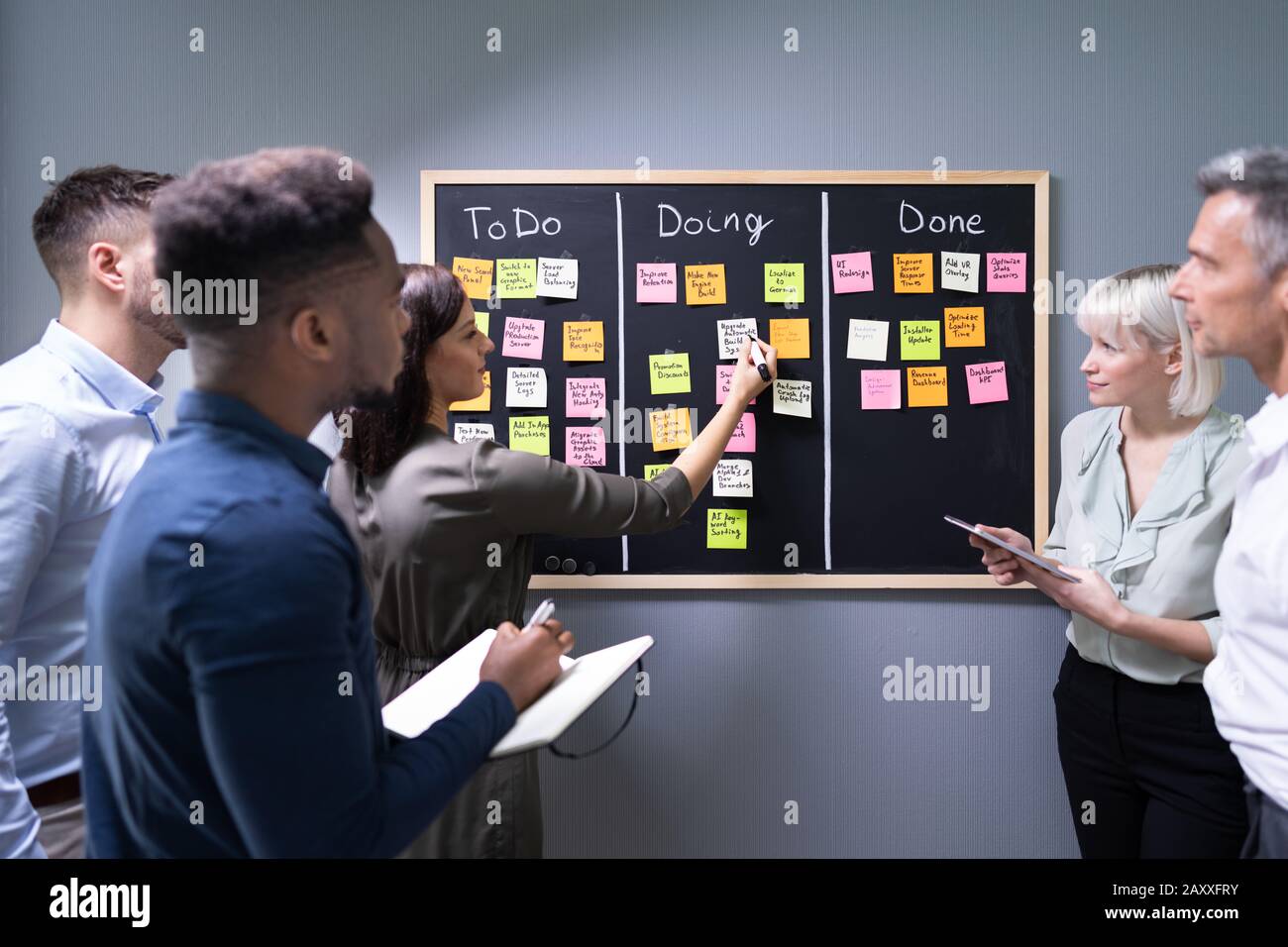 Group Of People Writing On Sticky Notes Attached To Blackboard In ...