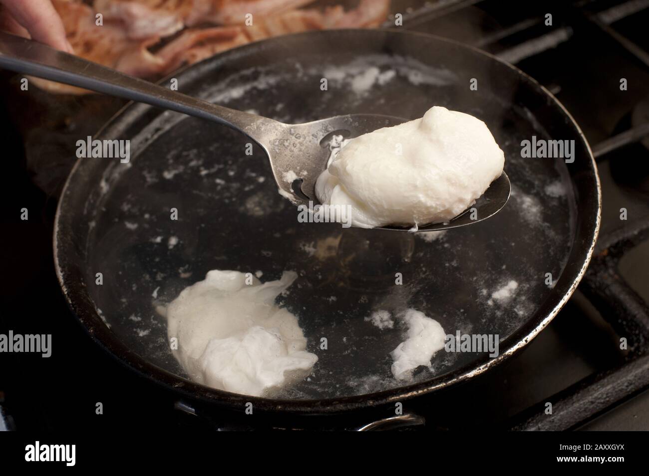 Person poaching eggs in boiling water in a frying pan over a gas hob ...