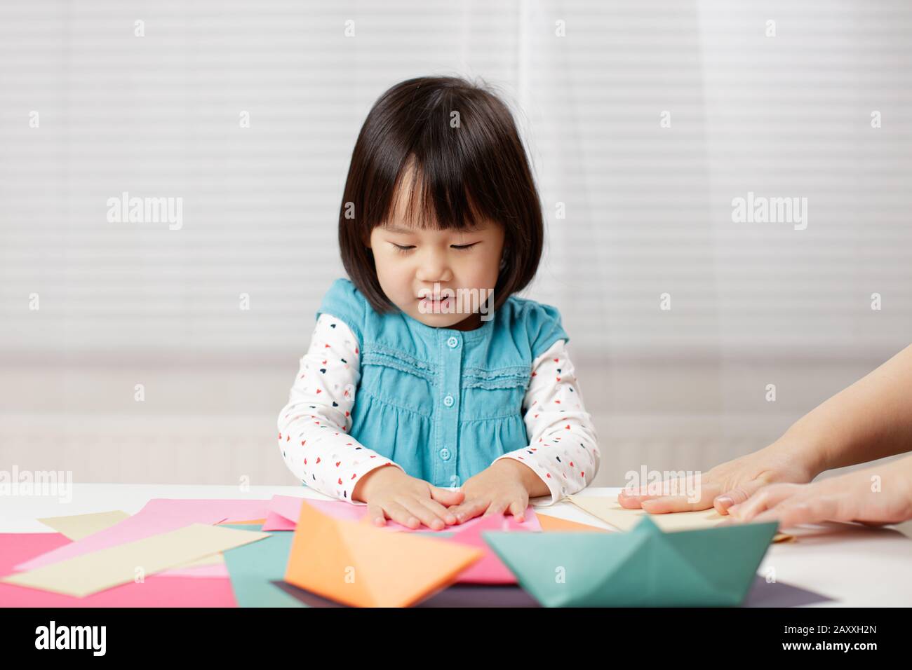 toddler girl learn making Origami at home against white background ...