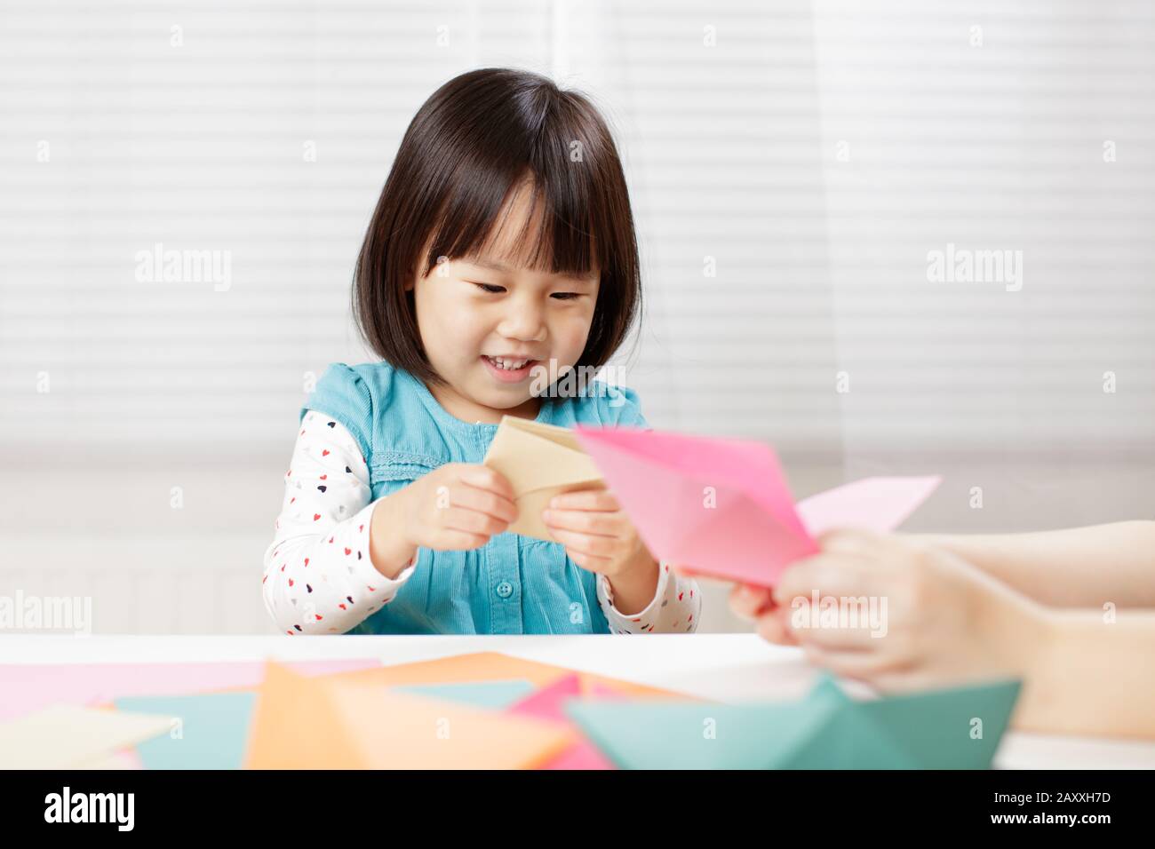 toddler girl learn making Origami at home against white background ...