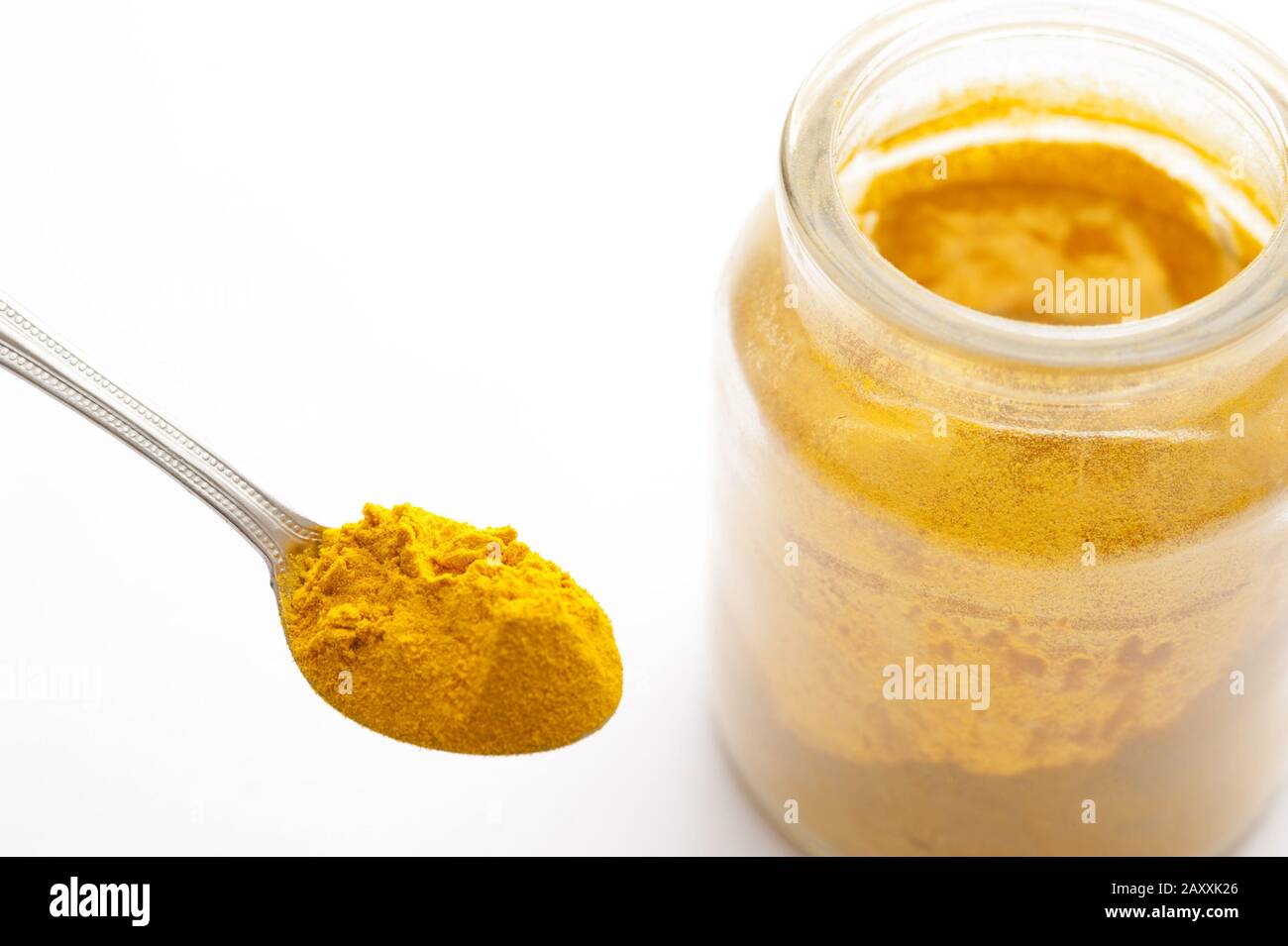A spoon and a jar of ground turmeric in close-up on white background ...