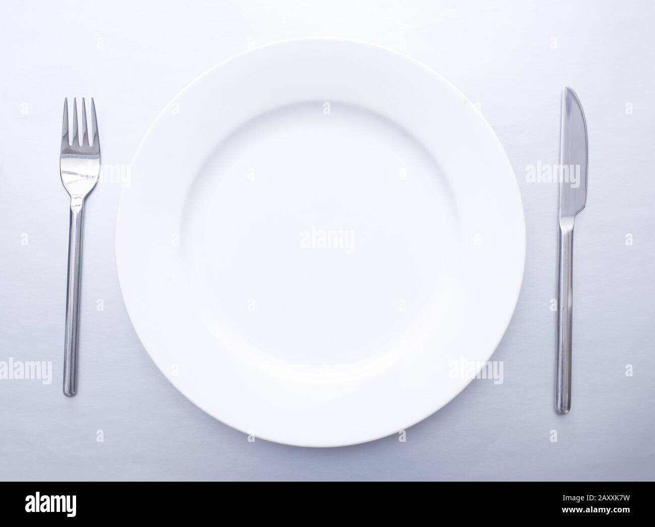 Plain simple place setting with empty white plate flanked by a silver ...
