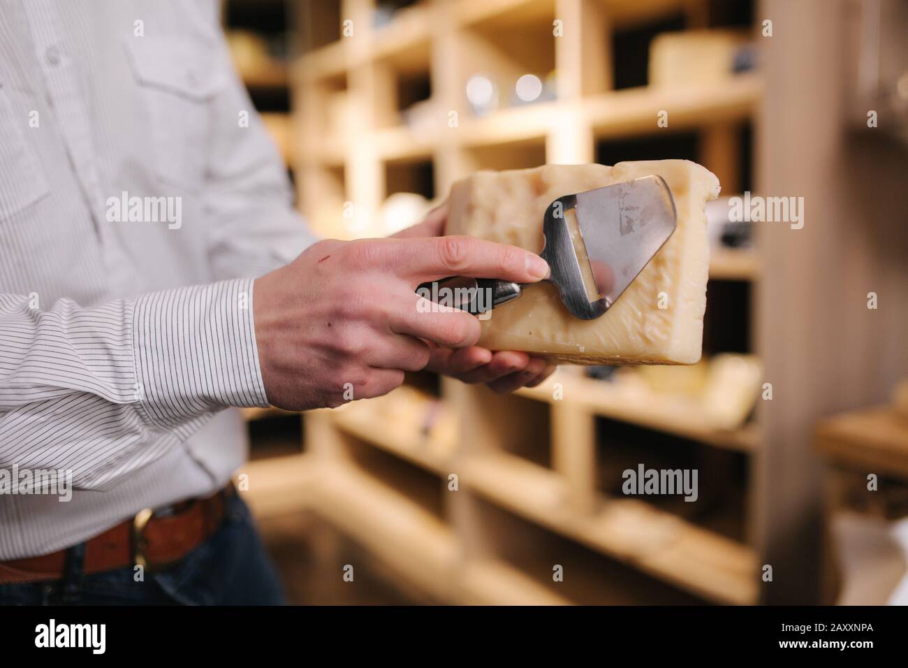 Man slicing little piece of cheese for taste. Young worker use special ...