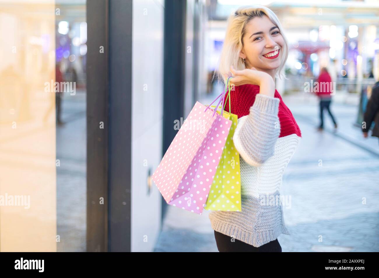 Back view of a smiling young woman standing and holding shop bags while ...