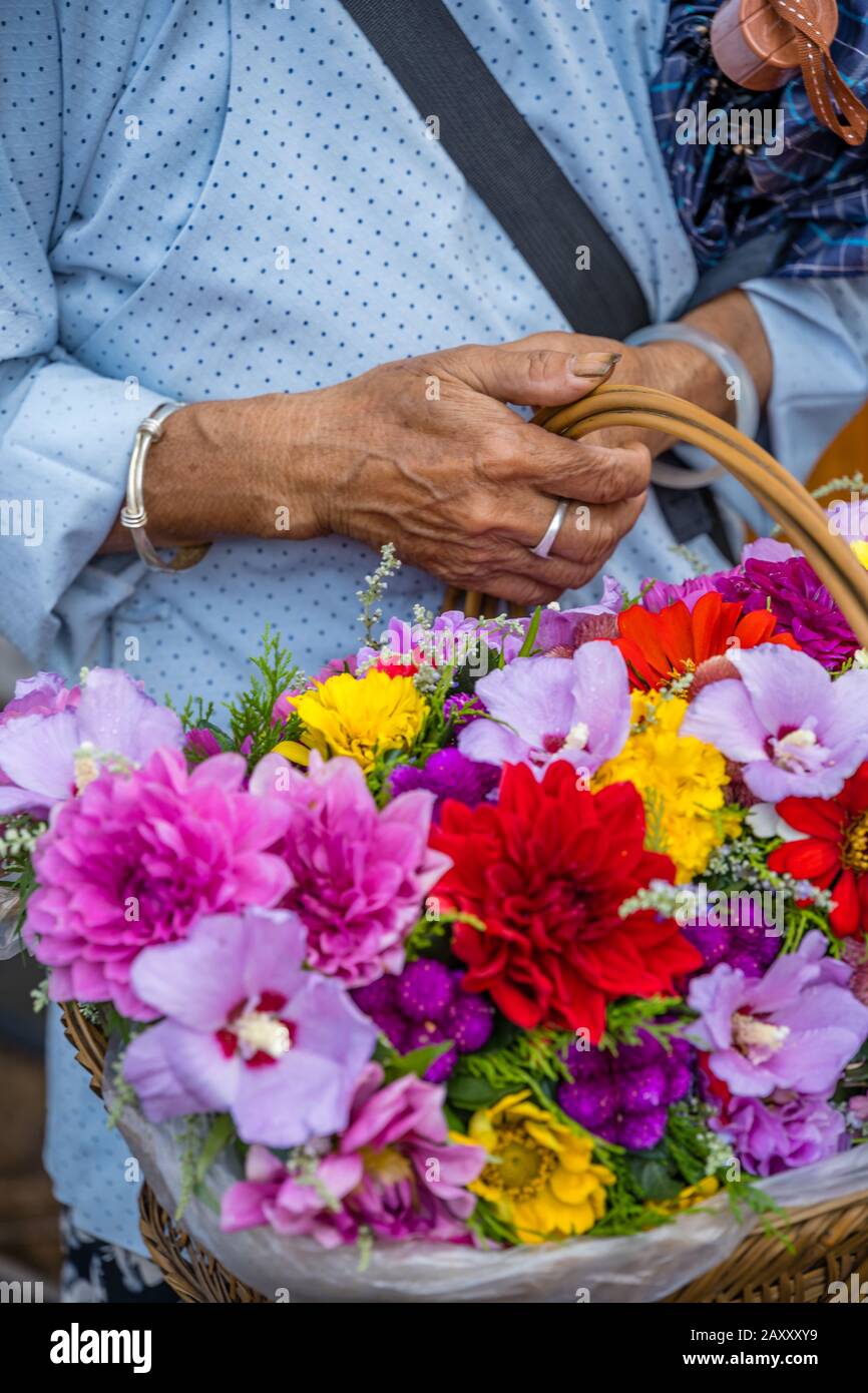 Old chinese woman selling flowers from a wicker basket on a street at ...