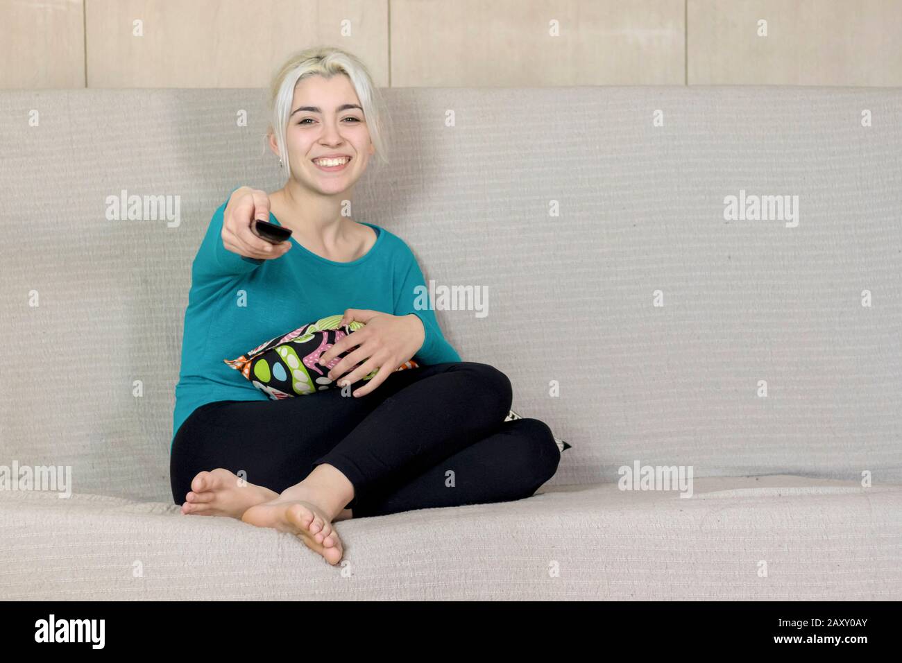 Smiling woman sitting on a couch with TV remote control at home Stock ...