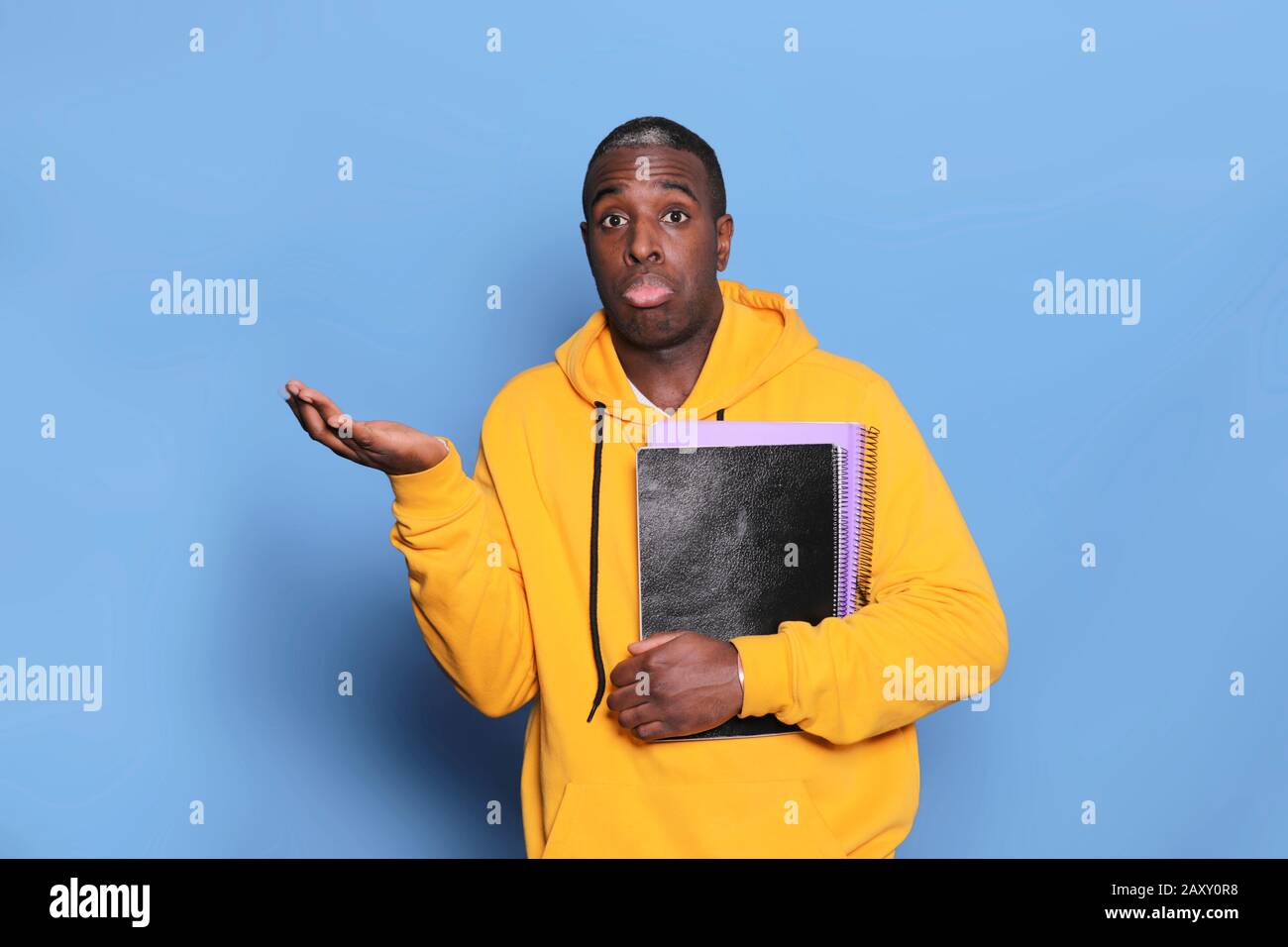 Confused black young man has hesitant expression, holds textbook ...
