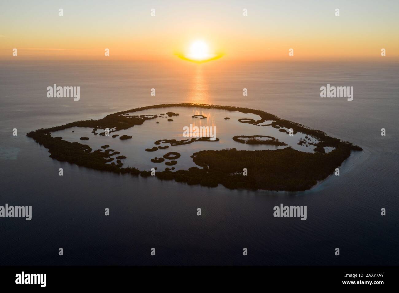 Seen at sunset, a remote tropical island, Kofiau, in the Molucca Sea is ...