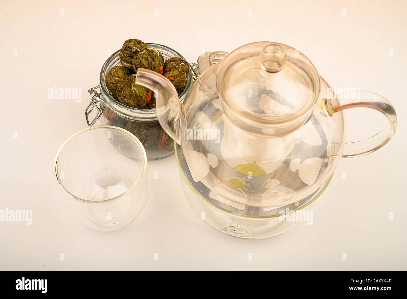 Flower tea balls in a glass jar, a glass teapot and a glass on a white ...