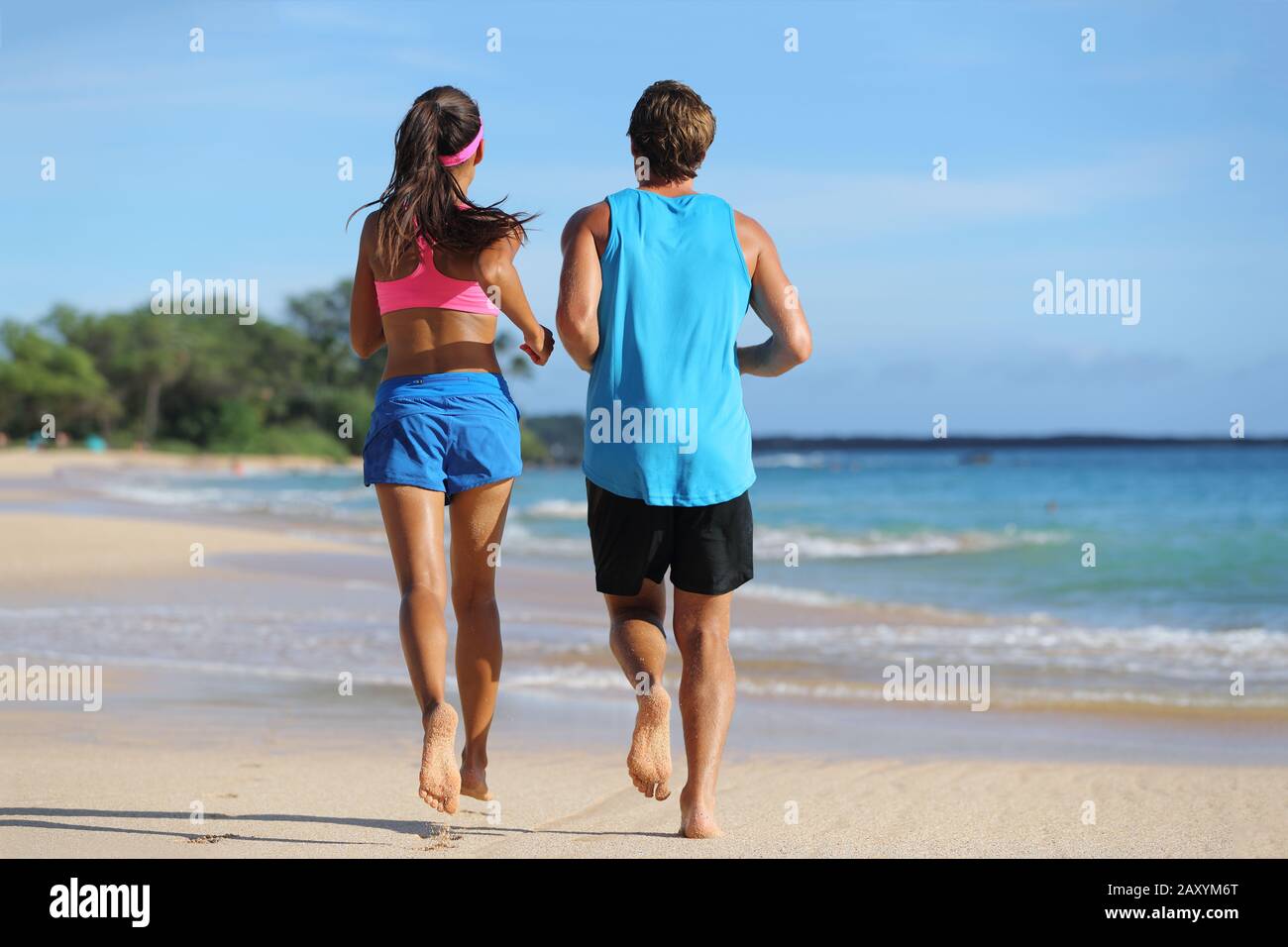 Two fitness athletes running together on beach. People from behind ...